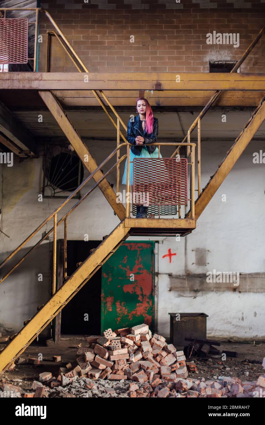 Portrait of a young girl with pink hair standing on the rusty stairs ...