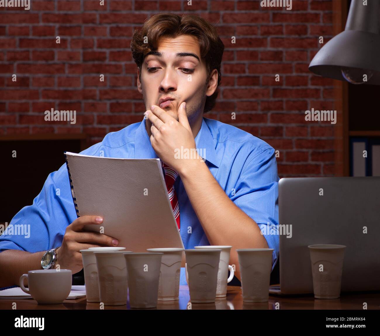 The young employee drinking coffee working at night shift Stock Photo ...