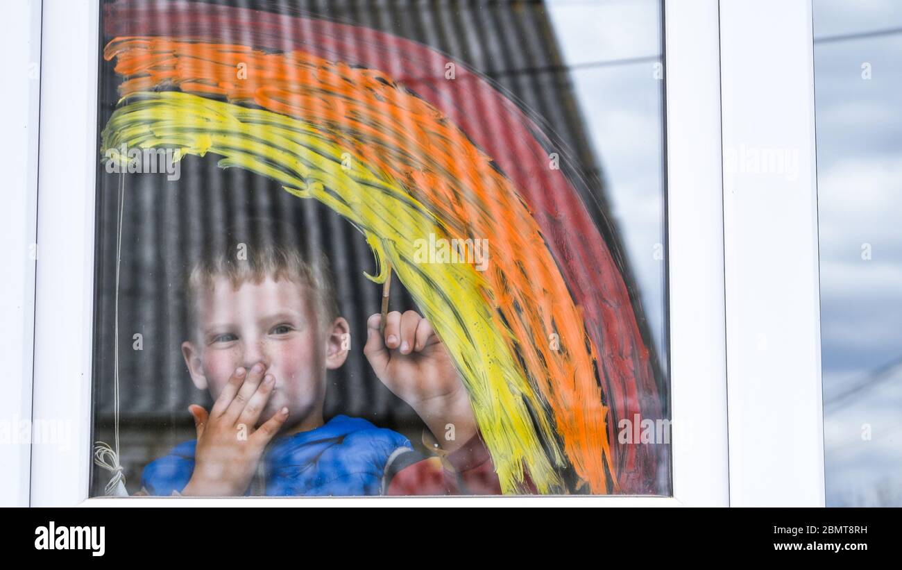 Little boy painting rainbow on a window and looking through the window ...