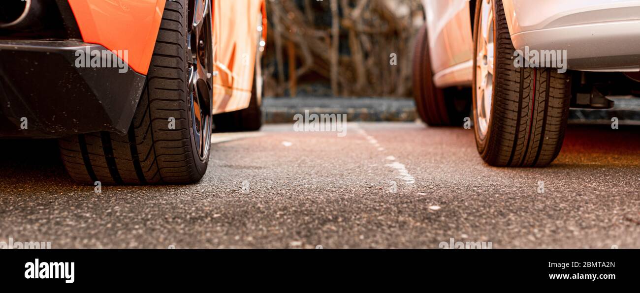 Back wheels of a supercar and a small car in a parking lot Stock Photo ...