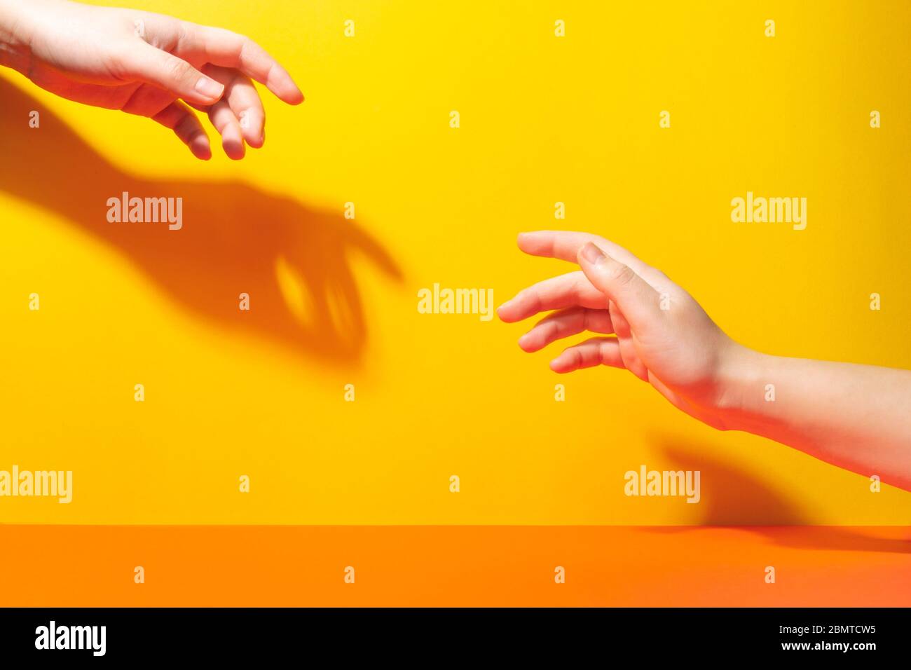 Two hands reach for each other with fingers. Shadows and hard light ...