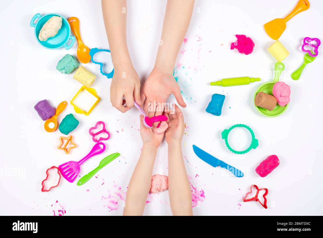 Two little girls play with modeling clay on white background. Top view ...