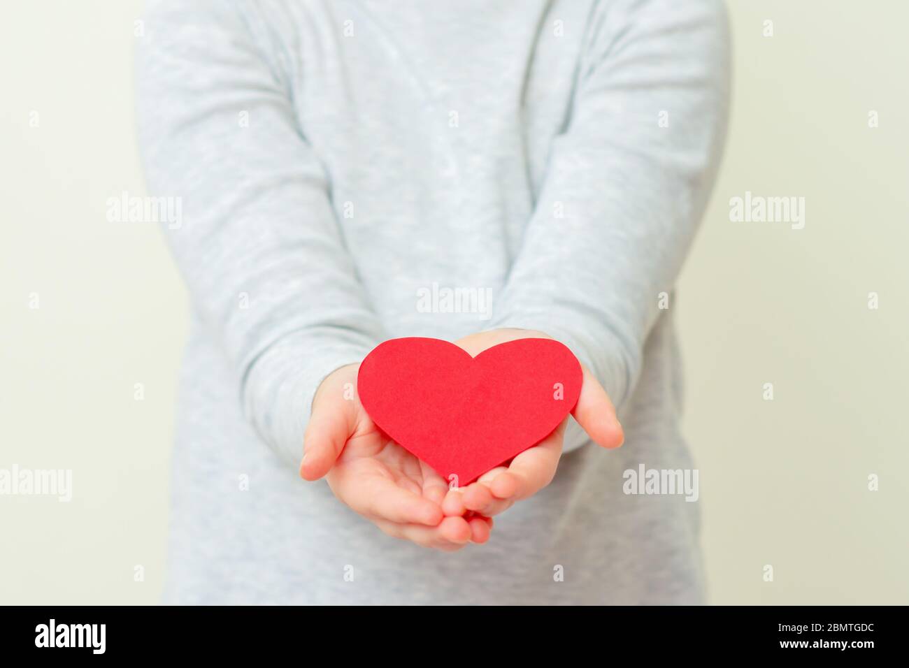 Closeup of hands of child holding red paper heart on white background ...