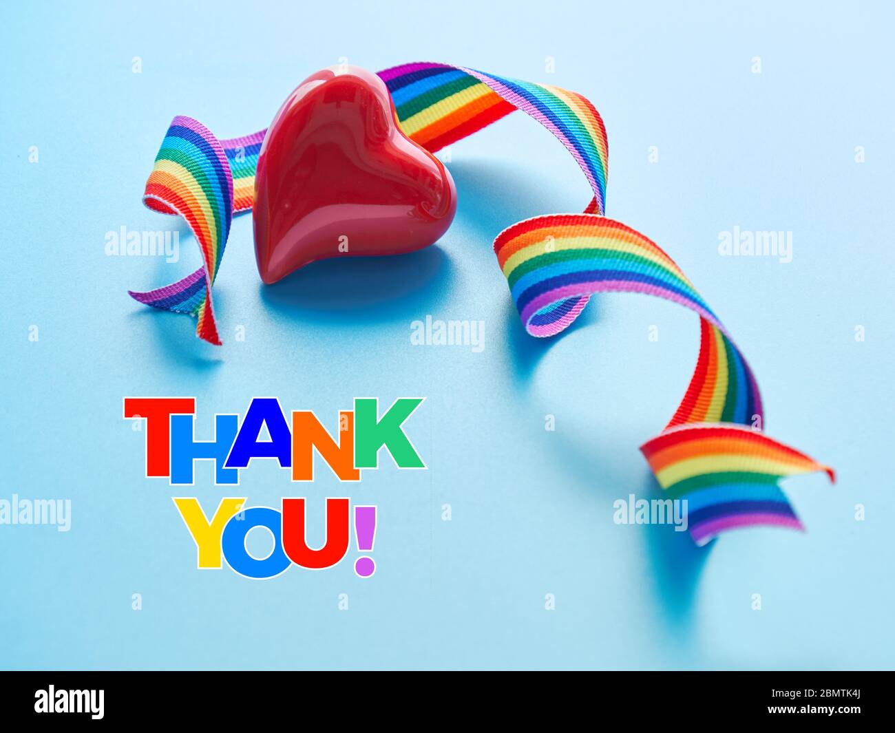 Red heart and curled rainbow ribbon. Rainbow text "Thank you" on blue ...