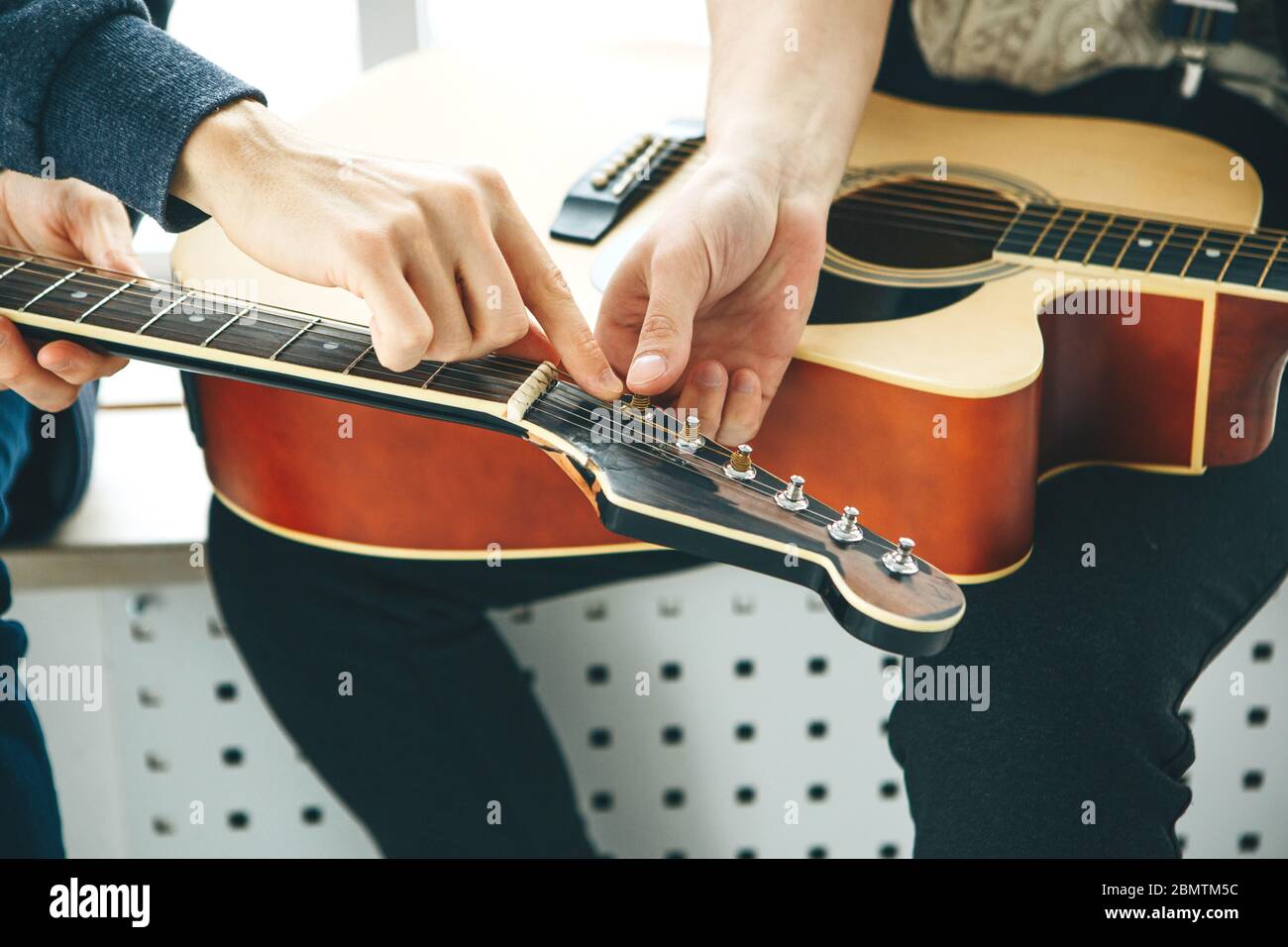 Learning to play the guitar. The teacher helps the student tune the ...