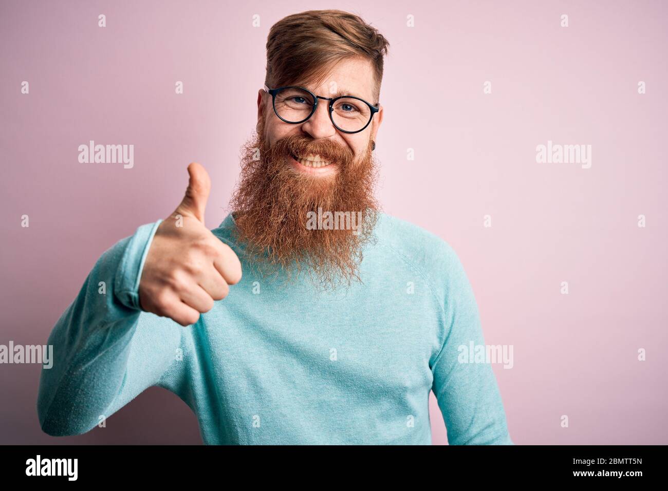 Handsome Irish redhead man with beard wearing glasses over pink ...