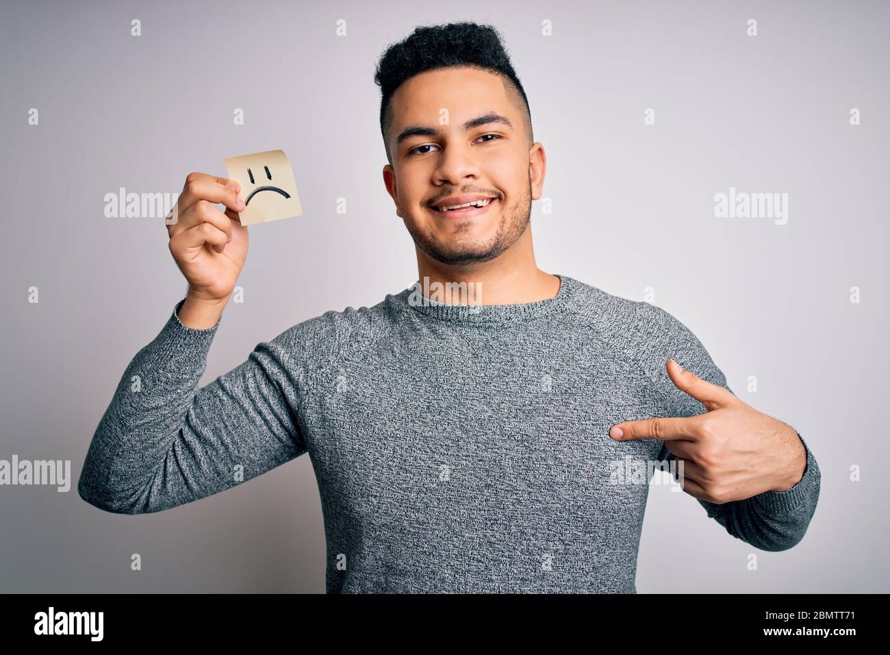 Handsome man holding reminder paper with sad emotion face emoji over ...