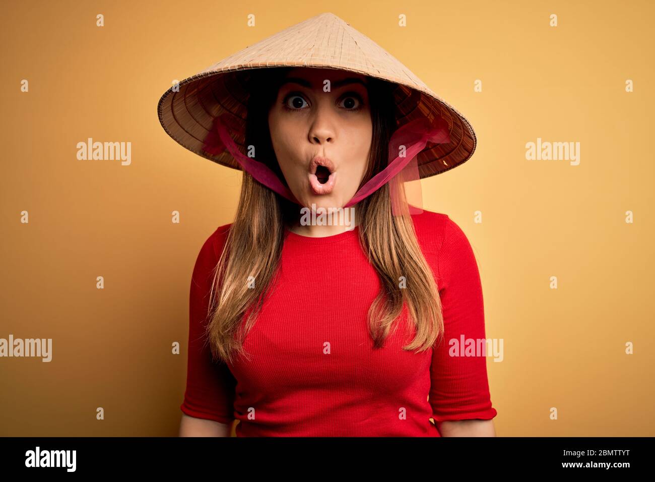 Young blonde woman wearing traditional asian rice paddy straw hat over ...