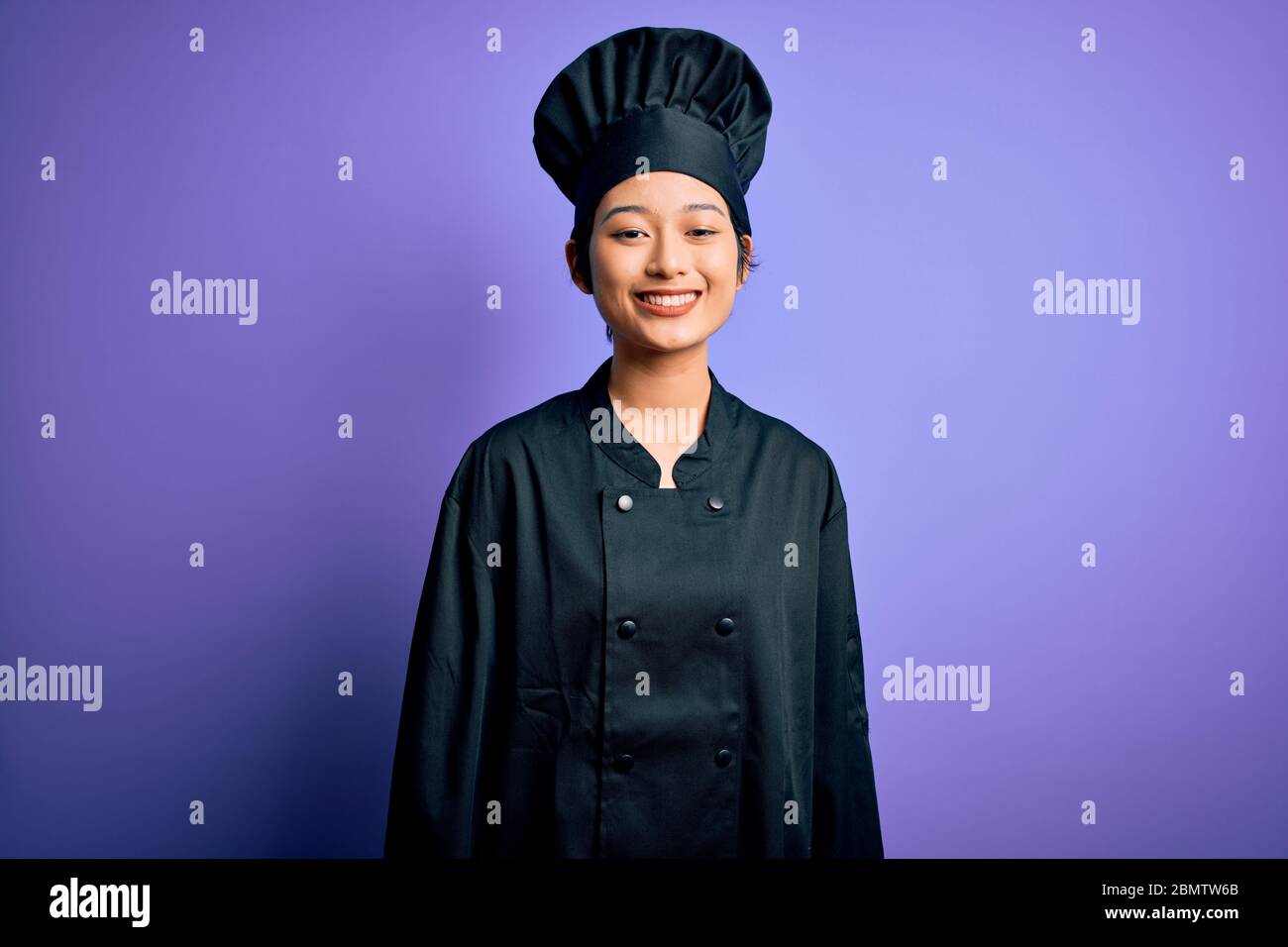 Young beautiful chinese chef woman wearing cooker uniform and hat over ...