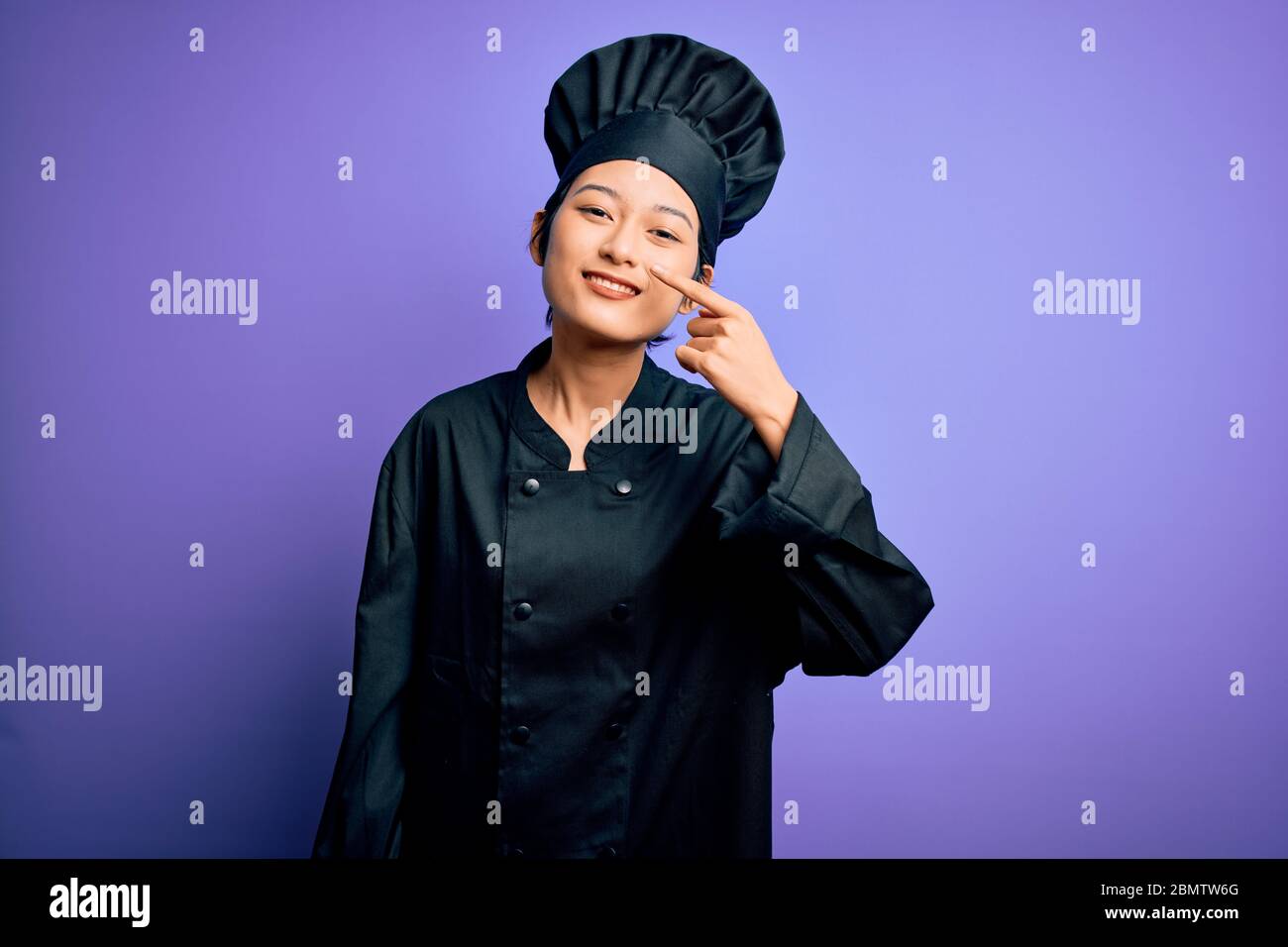 Young beautiful chinese chef woman wearing cooker uniform and hat over ...