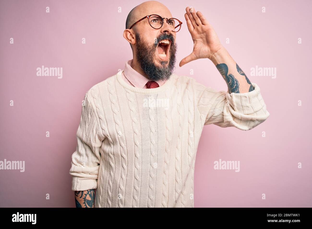 Handsome bald man with beard and tattoo wearing glasses and sweater ...