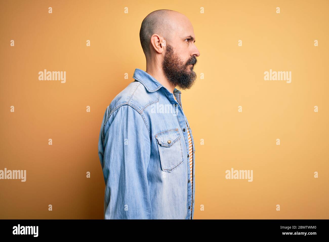 Handsome bald man with beard wearing casual denim jacket and striped t ...