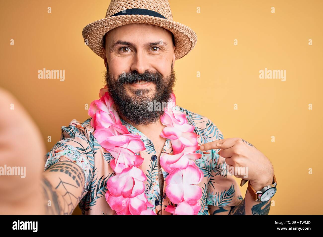 Handsome bald man with beard and tattoo on vacation wearing summer hat ...