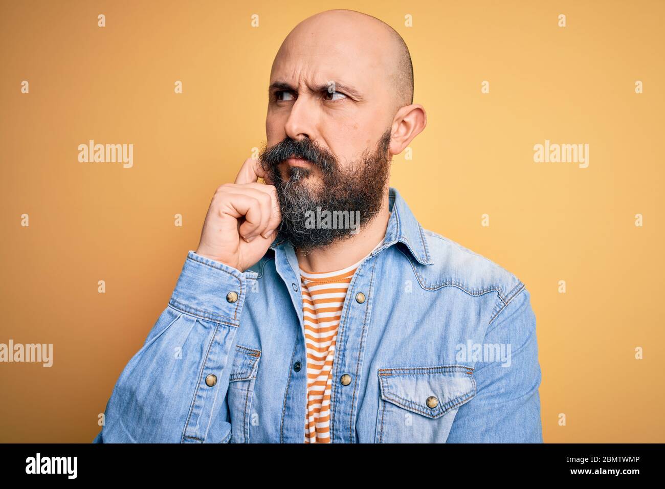 Handsome bald man with beard wearing casual denim jacket and striped t ...