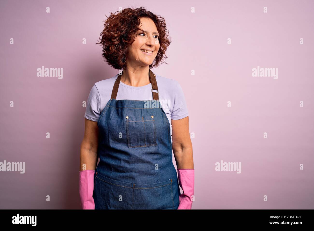 Middle age curly hair woman cleaning doing housework wearing apron and ...