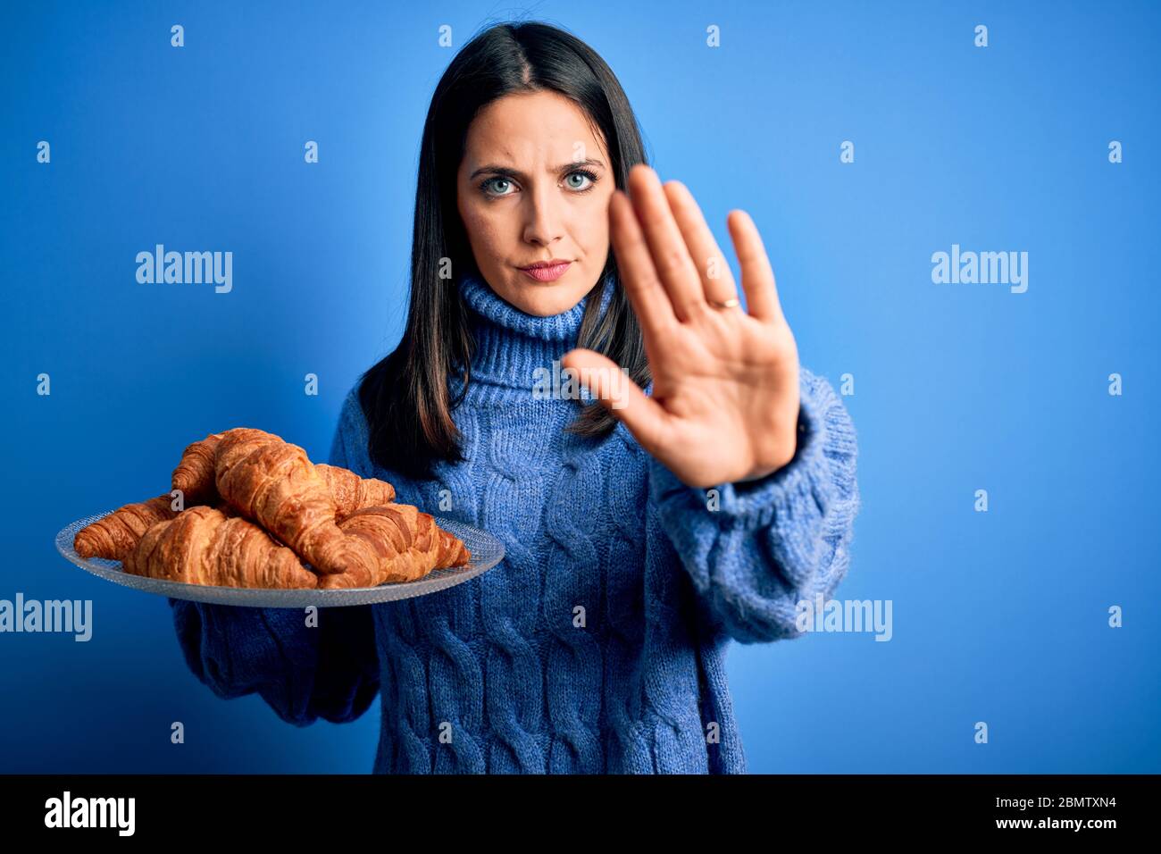 Young woman with blue eyes holding sweet croissants for breakfast over ...