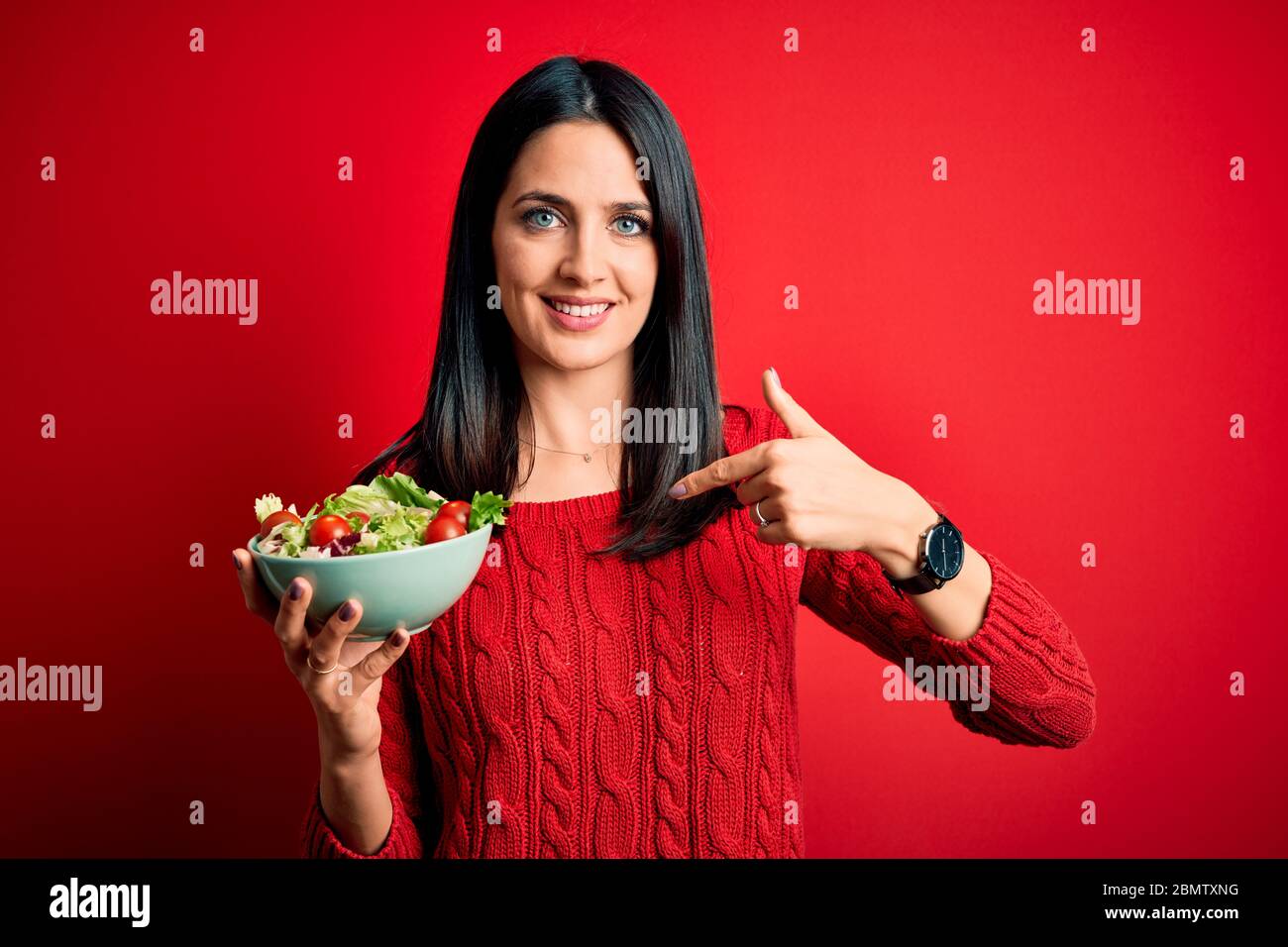 Young brunette woman with blue eyes eating healthy green salad over ...