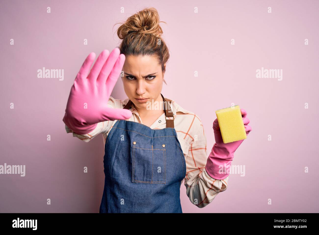 Beautiful blonde cleaner woman doing housework wearing arpon and gloves ...