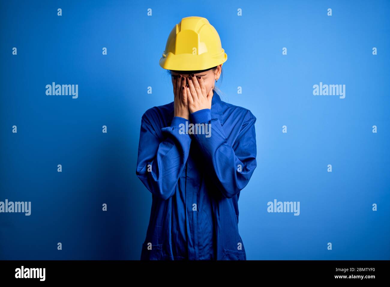 Young beautiful worker woman with blue eyes wearing security helmet and ...