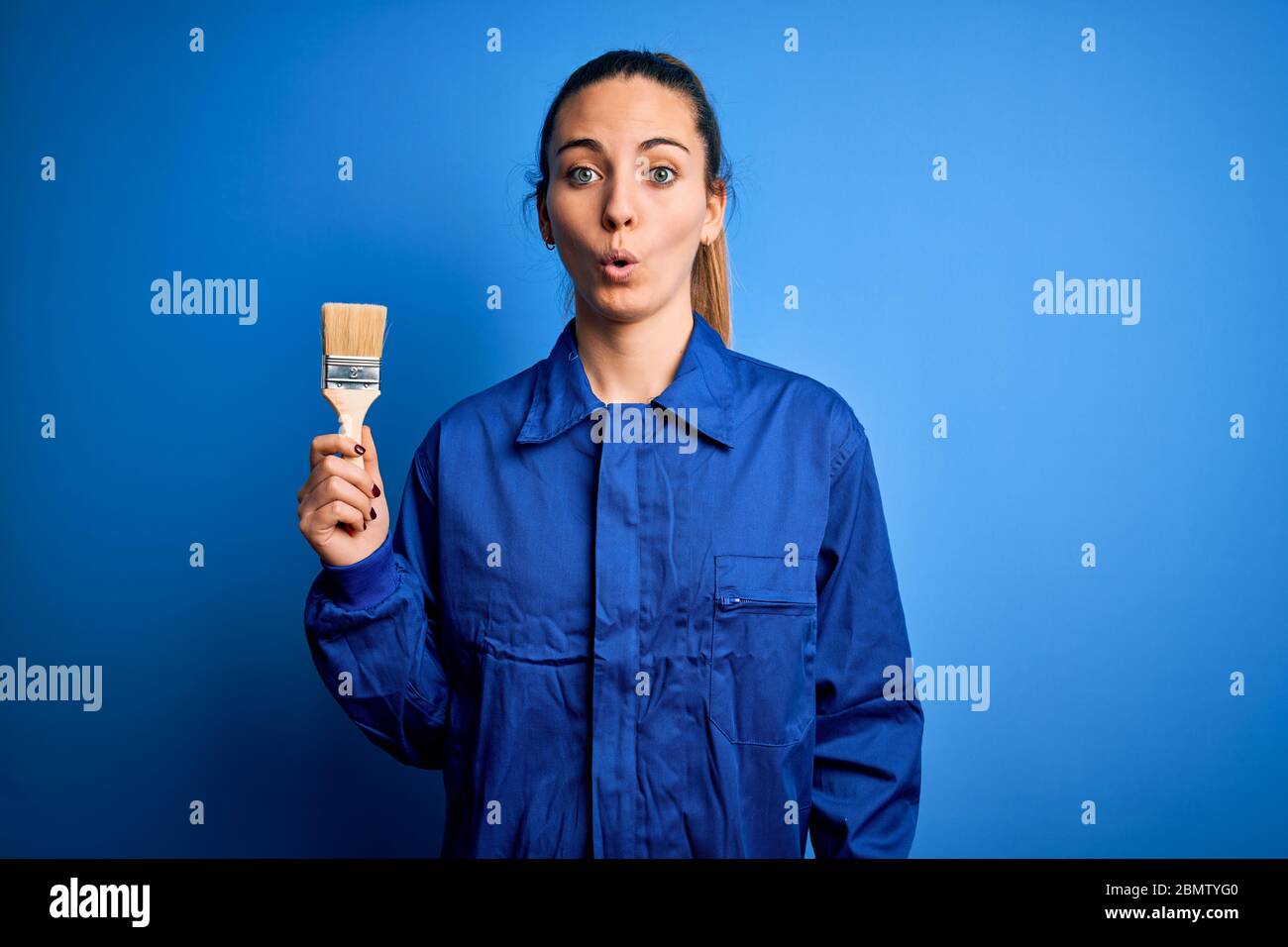 Young beautiful painter woman with blue eyes painting wearing uniform ...