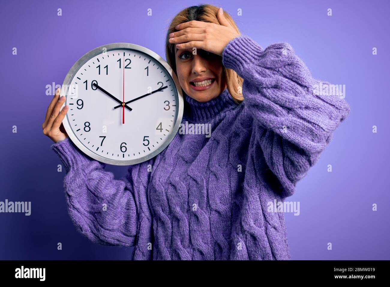 Young beautiful blonde woman doing countdown holding big clock over ...