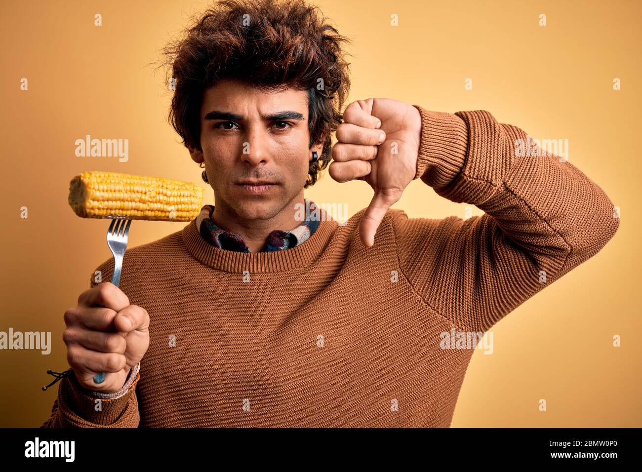 Young handsome man holding fork with cob corn standing over isolated ...