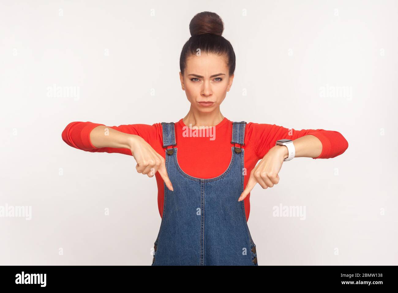 Do right now! Portrait of angry girl with hair bun in denim overalls ...