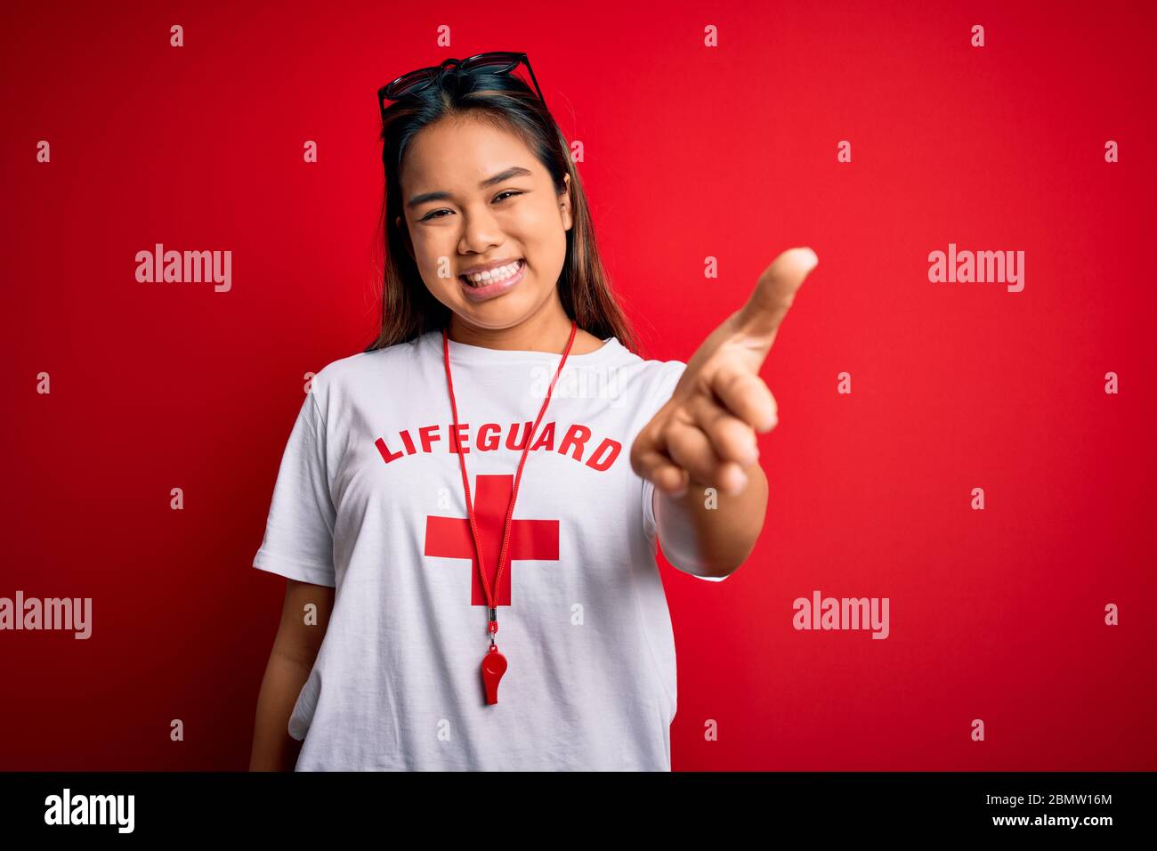Young asian lifeguard girl wearing t-shirt with red cross using whistle ...