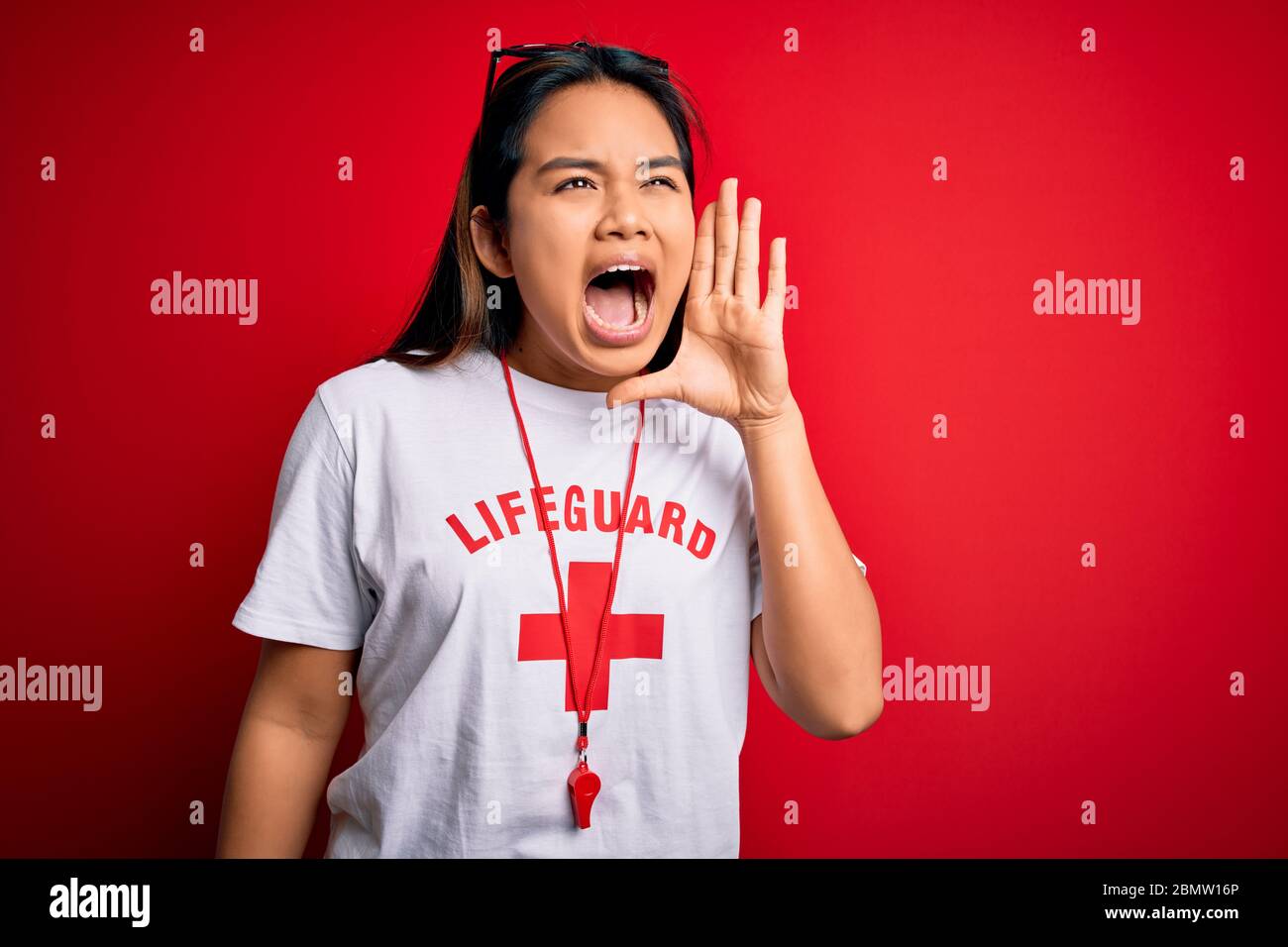 Young asian lifeguard girl wearing t-shirt with red cross using whistle ...