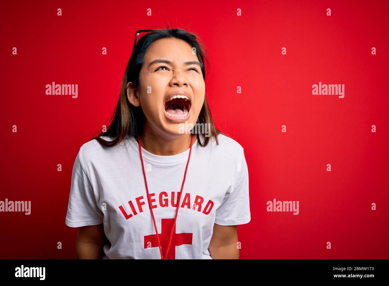 Young asian lifeguard girl wearing t-shirt with red cross using whistle ...