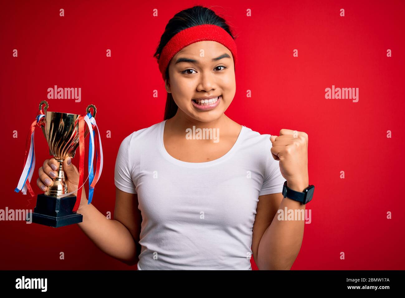 Young champion asian girl winning trophy cup standing over isolated red ...