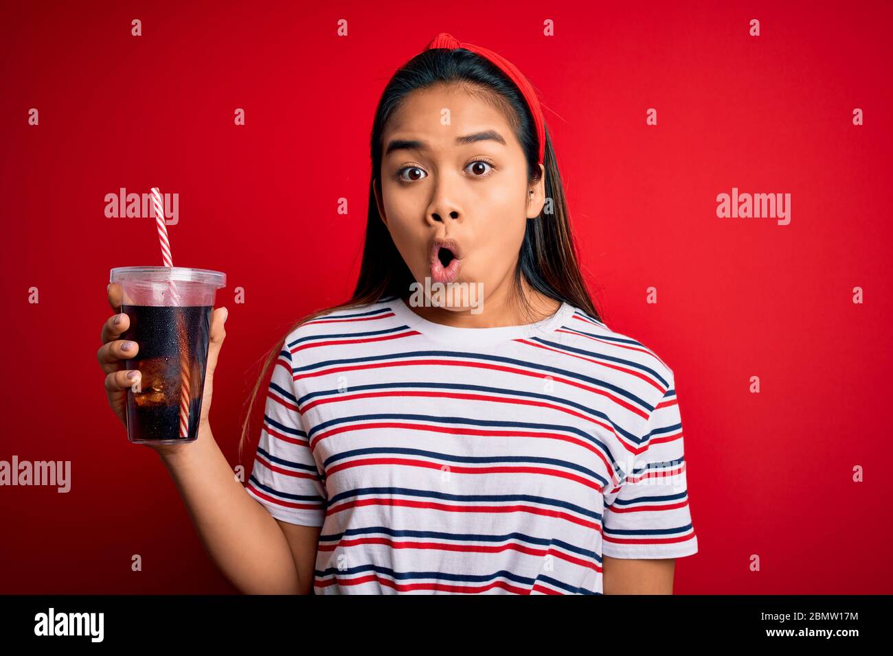 Young asian girl drinking cola fizzy refreshment using straw over ...