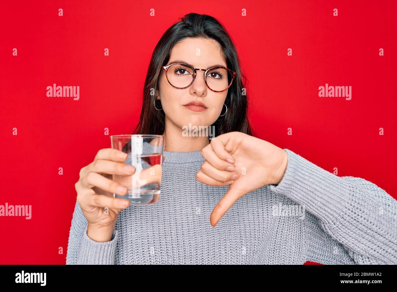 Young beautiful woman drinking a glass of fresh water over isolated red ...