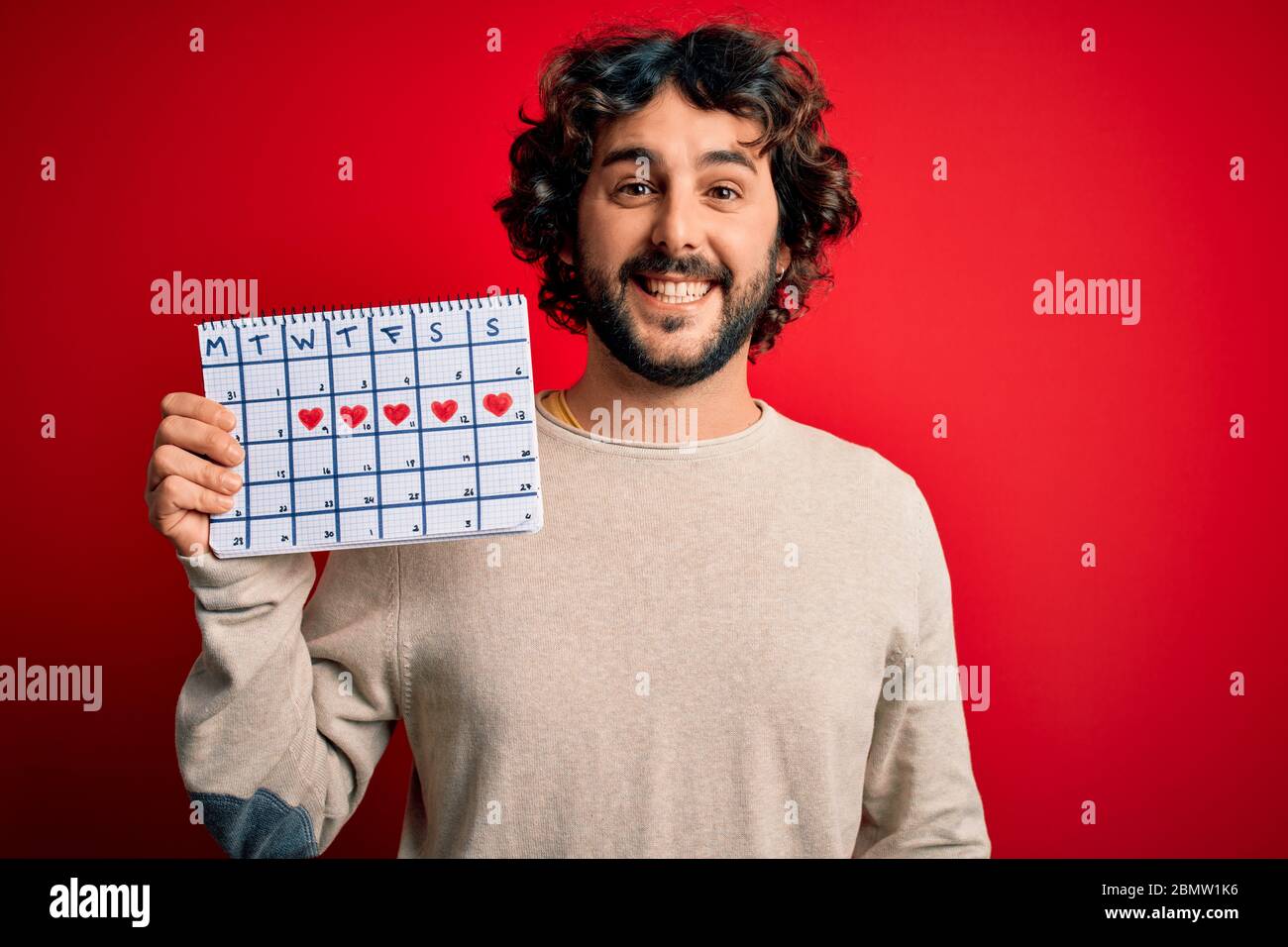 Young handsome man with beard holding calendar over isolated red ...