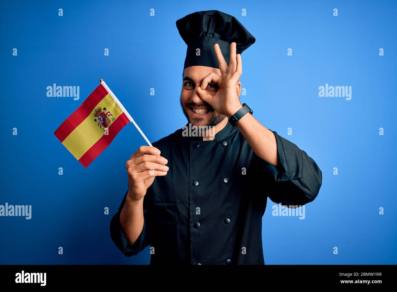 Young handsome cooker man with beard wearing uniform holding spain ...