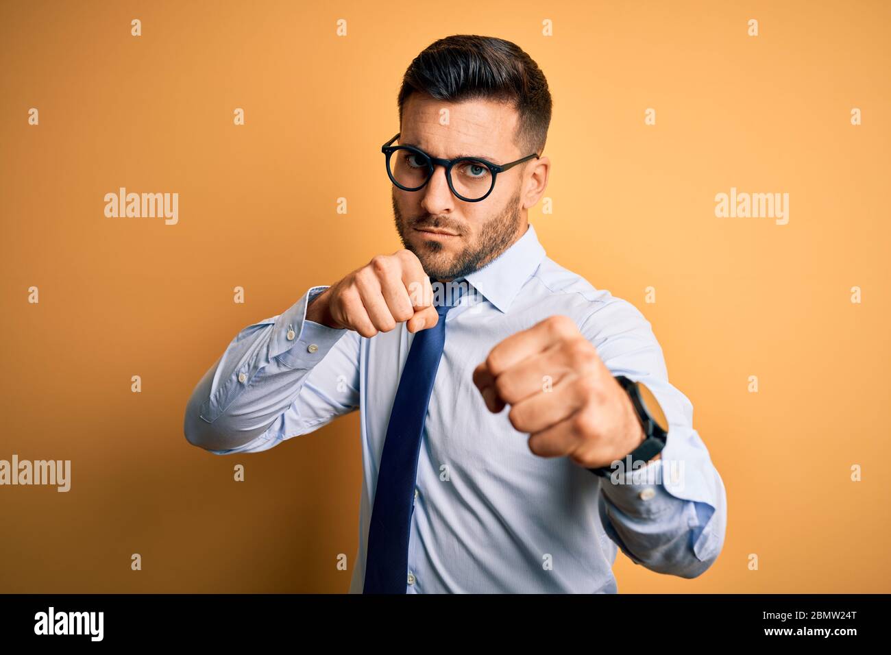 Young handsome businessman wearing tie and glasses standing over yellow ...