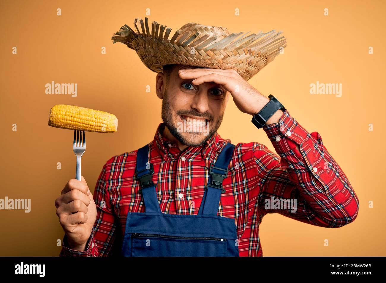 Young rural farmer man holding countryside corn over isolated yellow ...