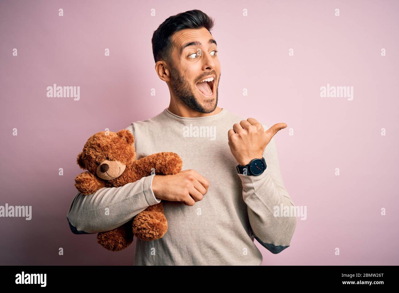 Young handsome man holding teddy bear standing over isolated pink ...