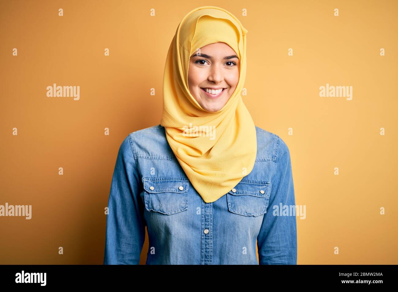 Young beautiful girl wearing muslim hijab standing over isolated yellow ...