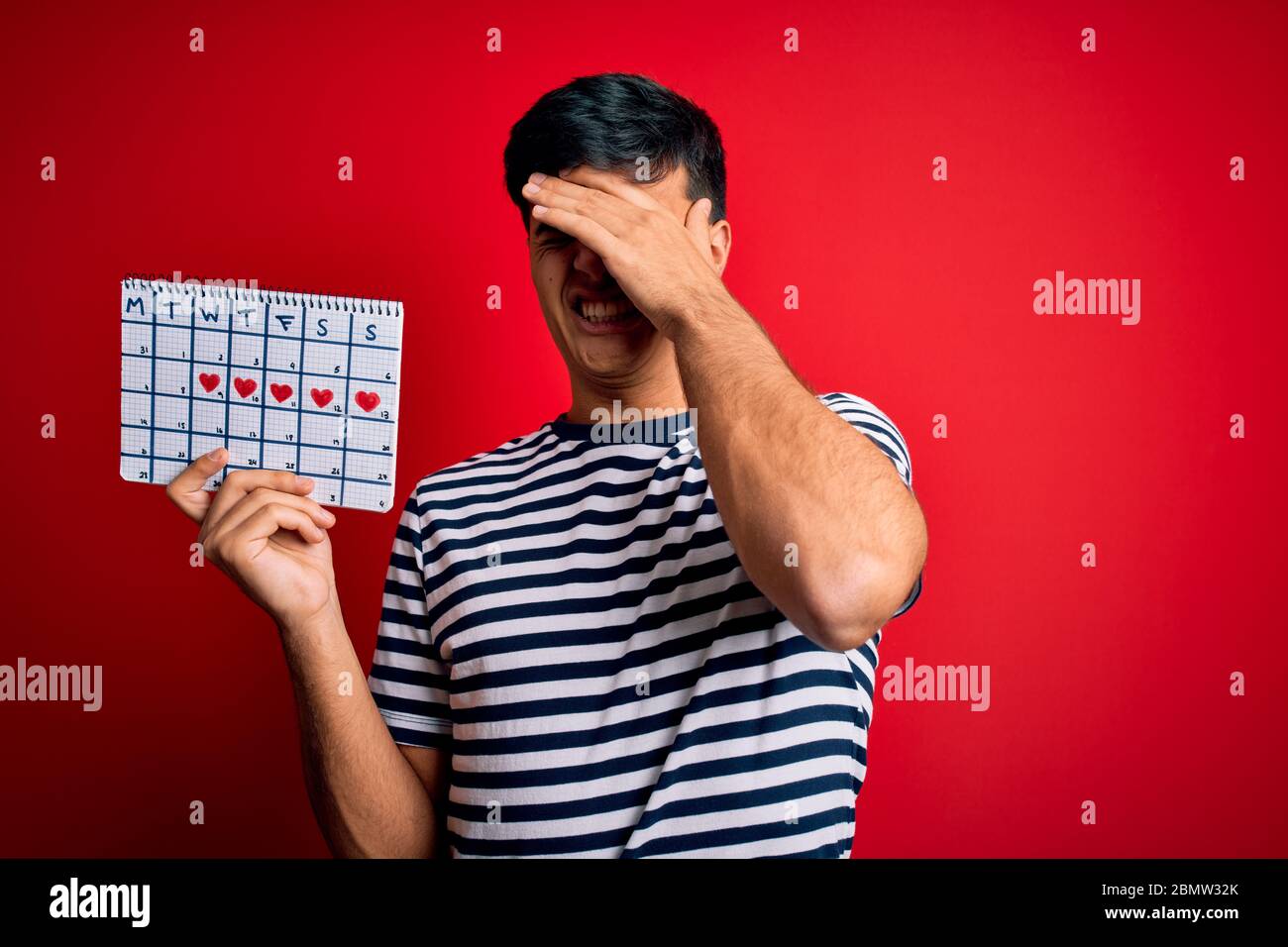 Young handsome man holding calendar with hearts over isolated red ...
