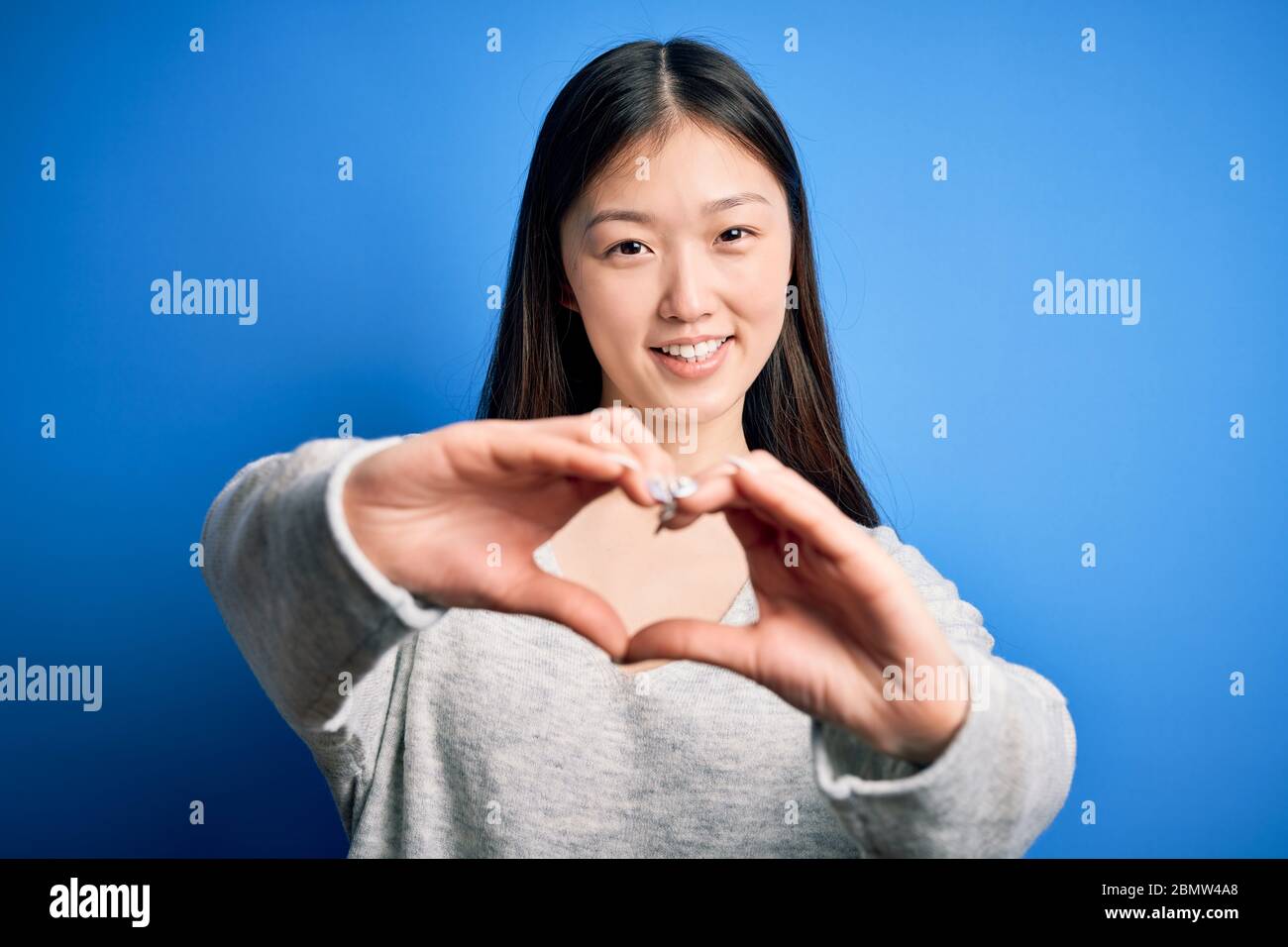 Young beautiful asian woman wearing casual sweater standing over blue ...