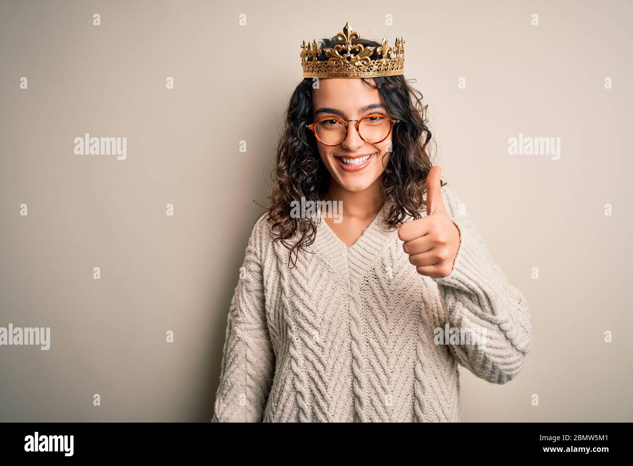 Young beautiful woman with curly hair wearing golden queen crown over ...