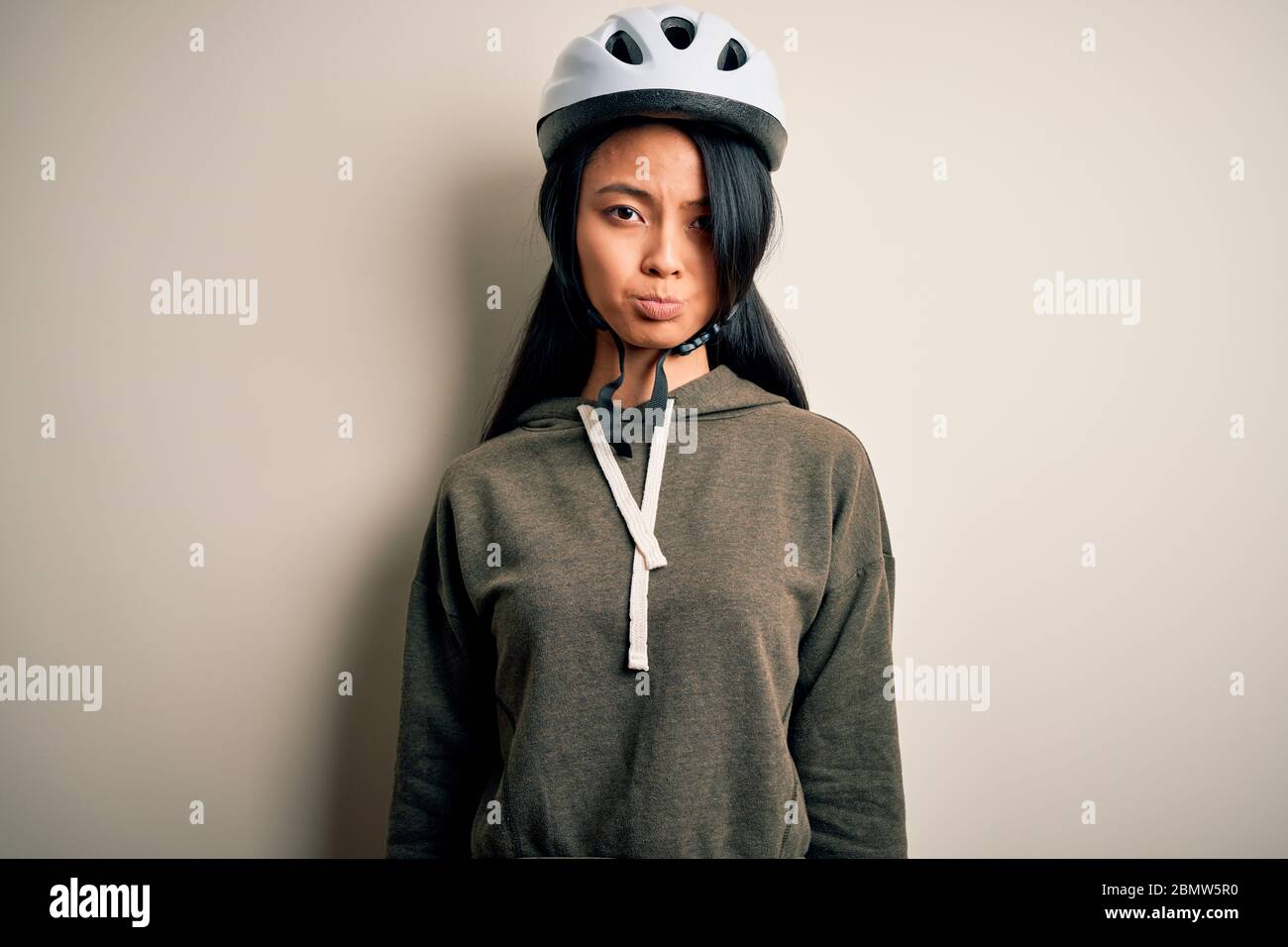Young beautiful chinese woman wearing bike helmet over isolated white background depressed and ...