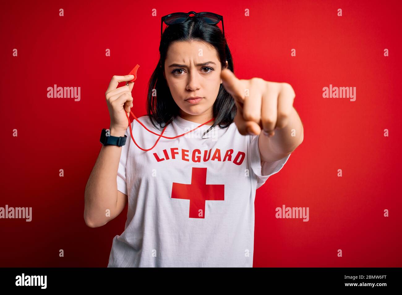 Young lifeguard woman wearing guard equipement holding whistle over red ...