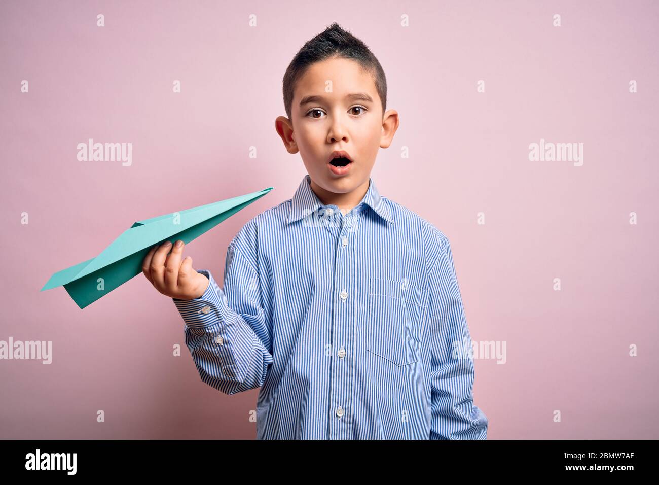 Young little boy kid holding paper plane over isolated pink background ...