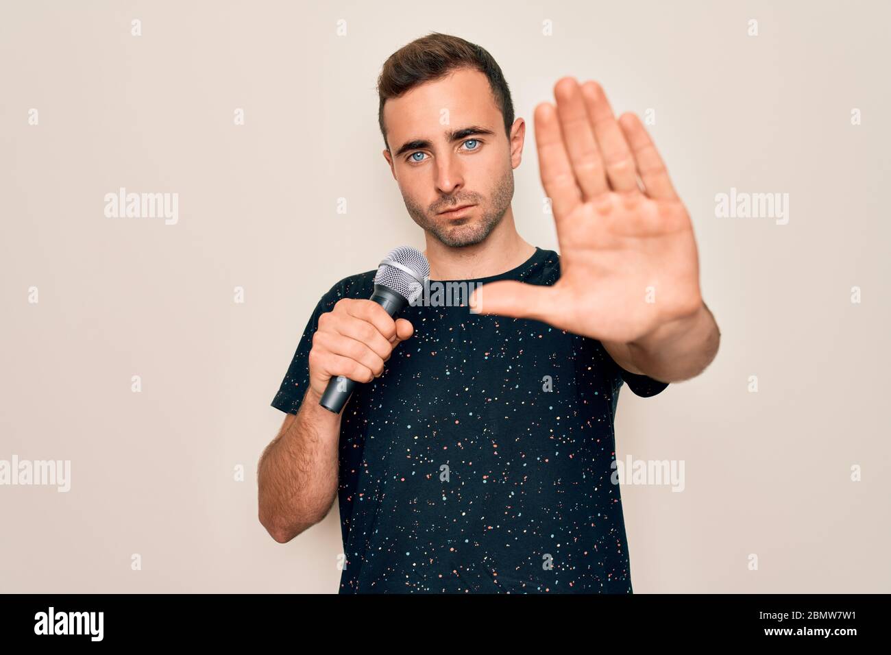Young handsome singer man with blue eyes singing using microphone over white background with ...