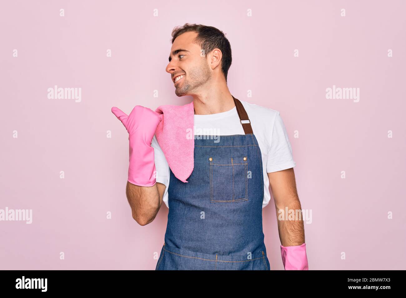 Young cleaner man with blue eyes cleaning wearing apron and gloves over ...