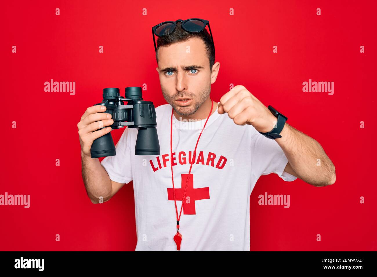 Young handsome lifeguard man wearing t-shirt with red cross and whistle ...