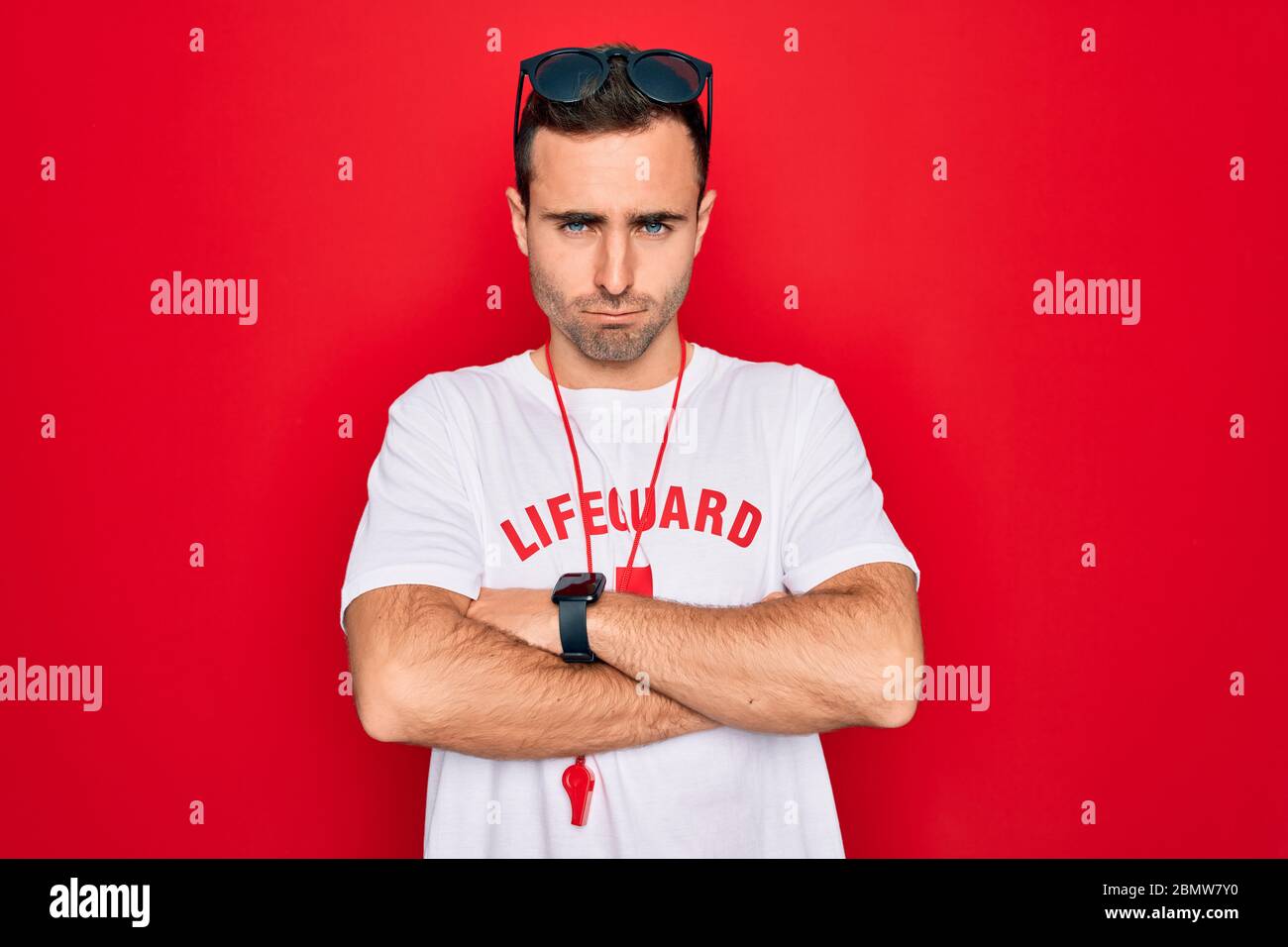 Handsome lifeguard man wearing t-shirt with red cross and whistle over ...