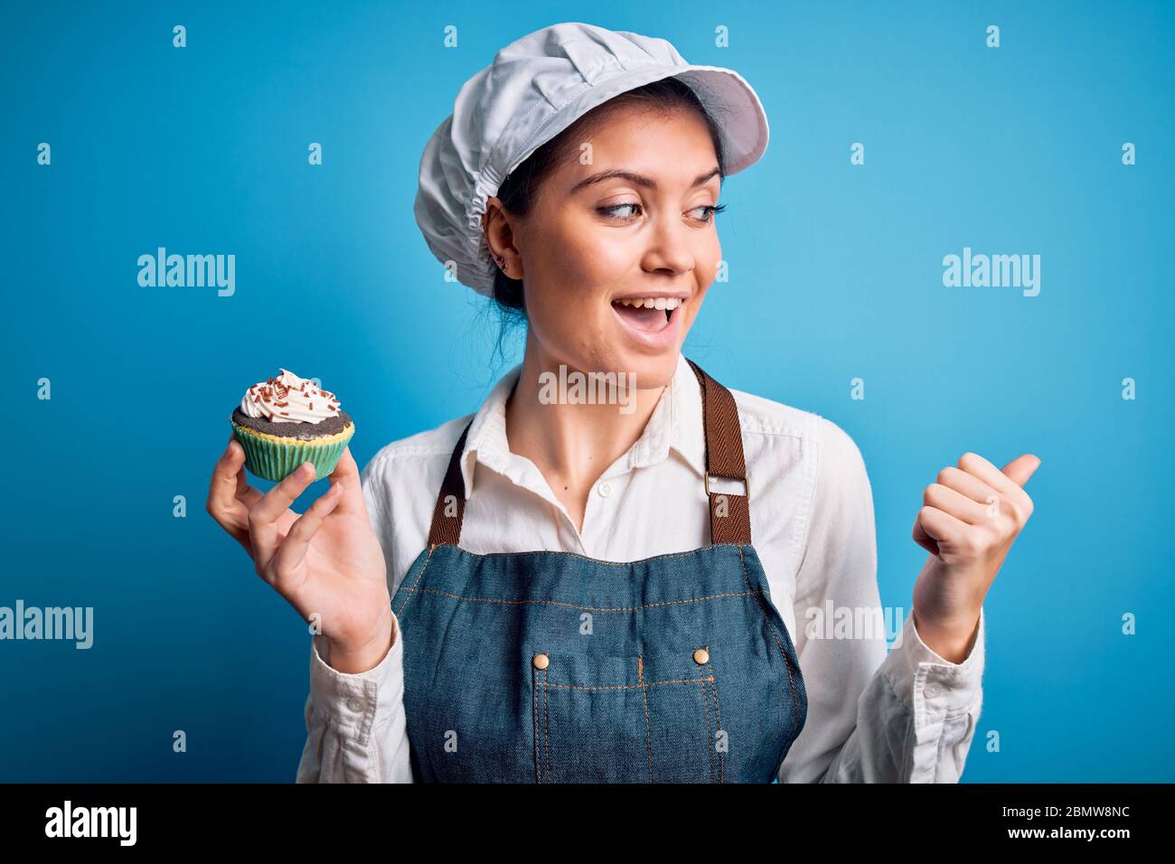 Young beautiful baker woman with blue eyes wearing apron holding ...